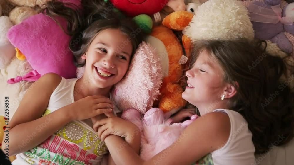 Two little friends chat and laugh, lying in the bed covered of lots of ...