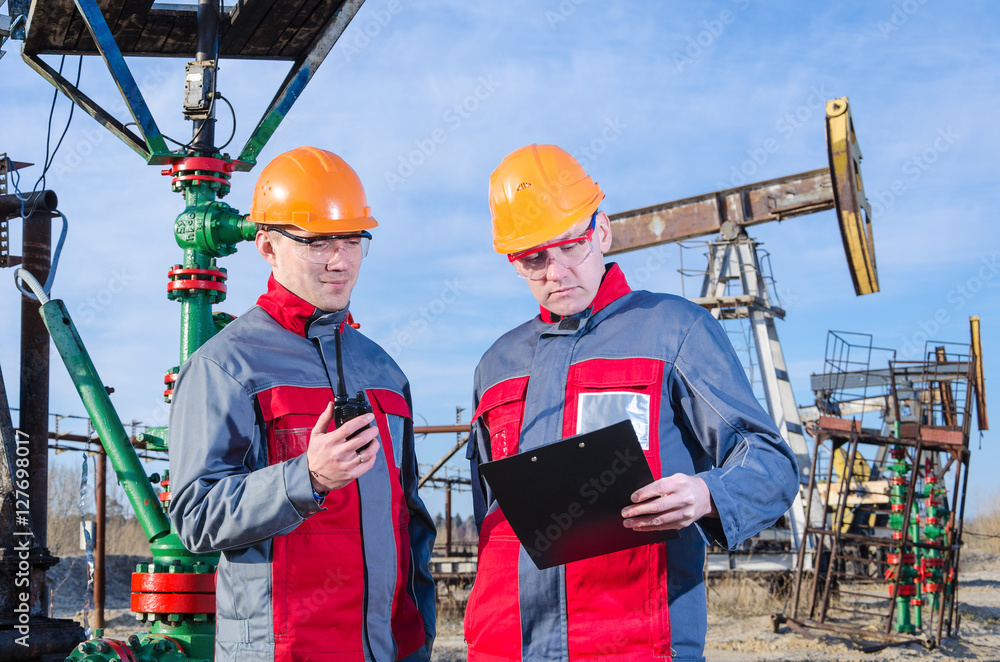 Two workers in the oilfield checking test results. Pump jack and ...