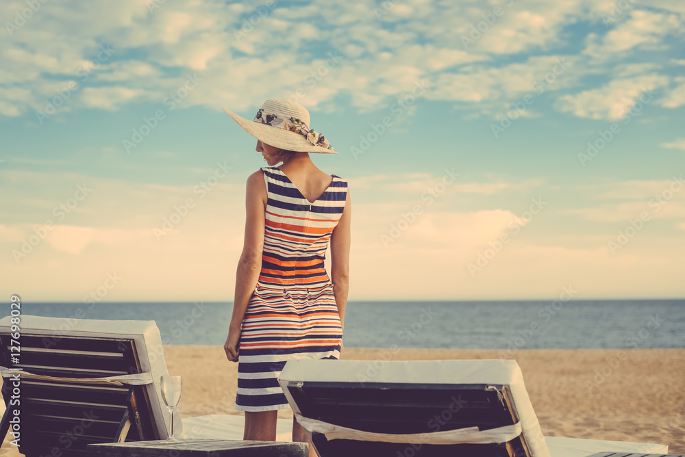 Back view of elegant lady relaxing on a chaise lounge, sandy beach ...