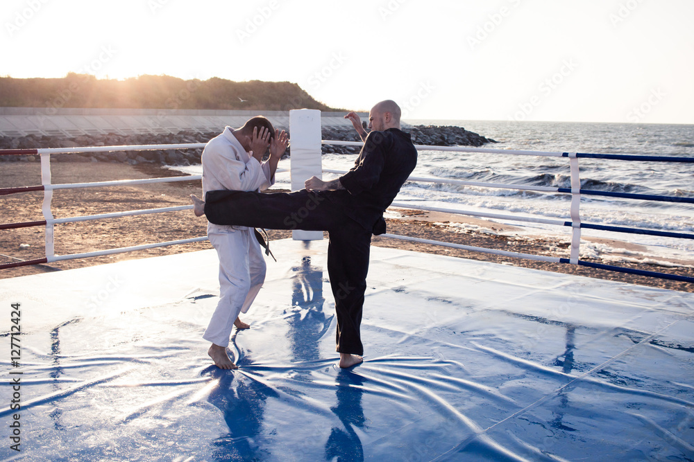 Two professional male karate fighters are fighting on the beach boxing ...