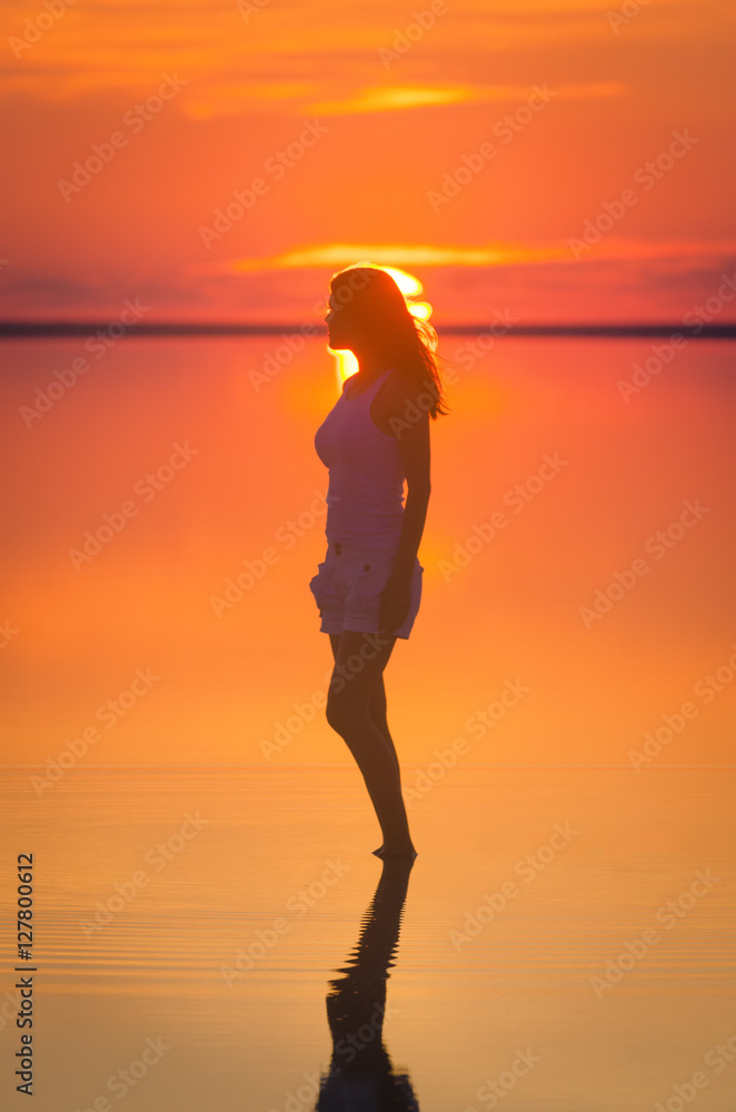 Beautiful female model stands in front of sun goes behind horizon at ...