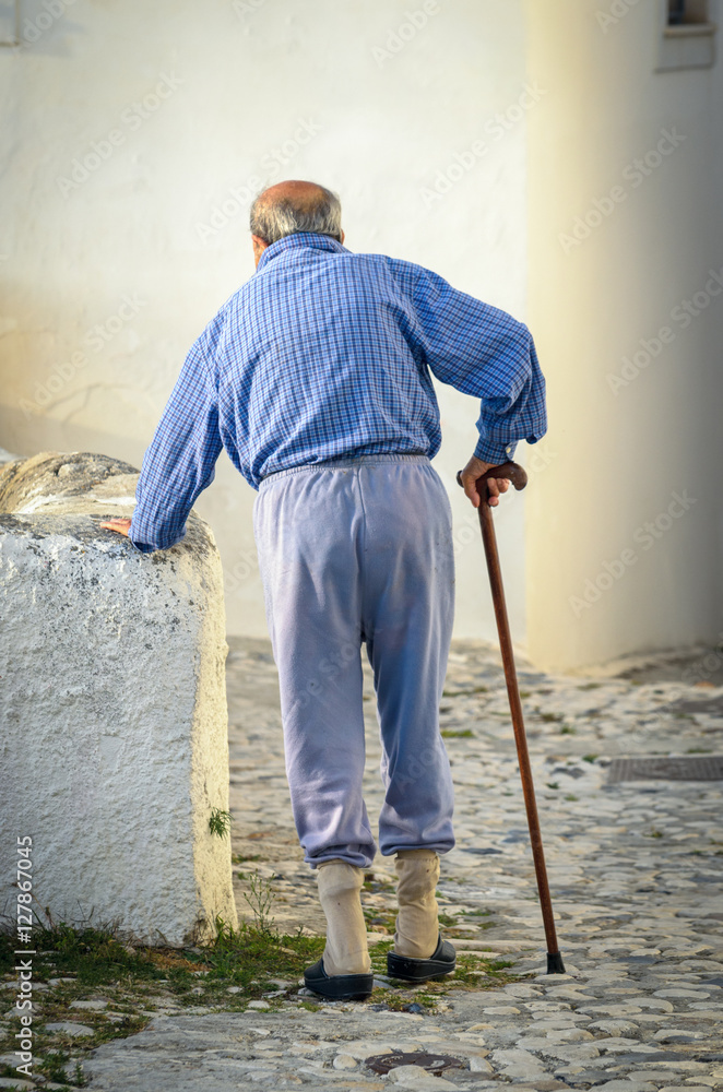 Old tired man with a walking stick shooted from behind elderly concept ...