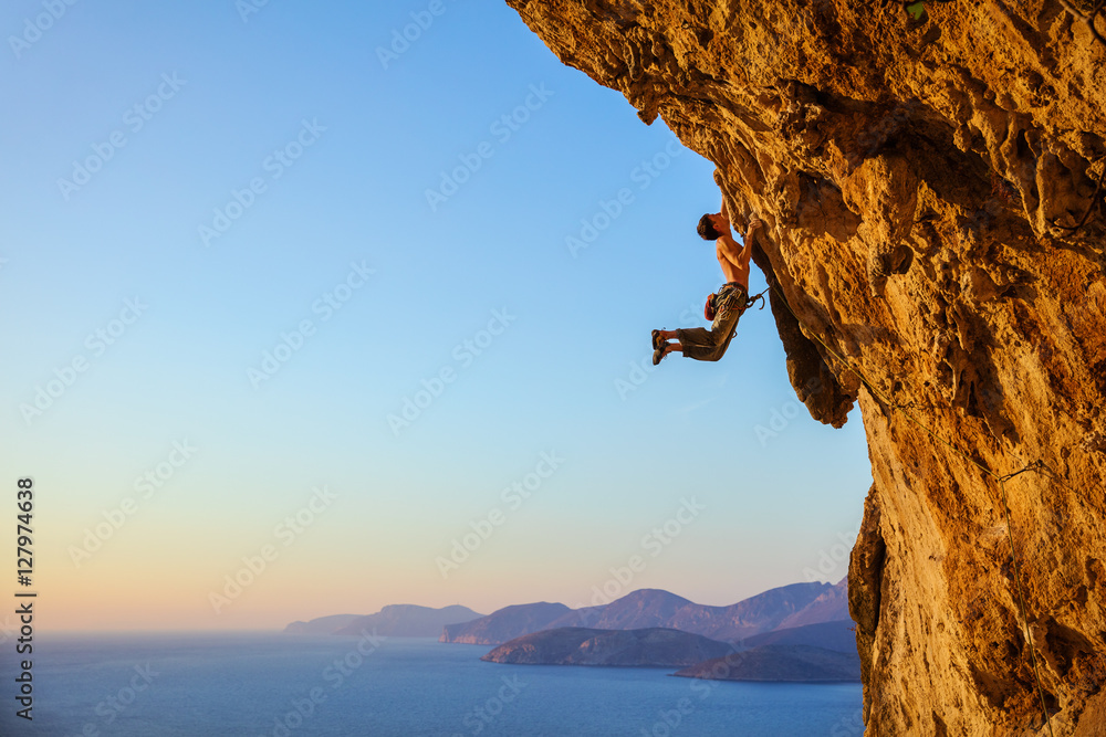 Rock climber jumping on handholds while climbing overhanging cliff ...