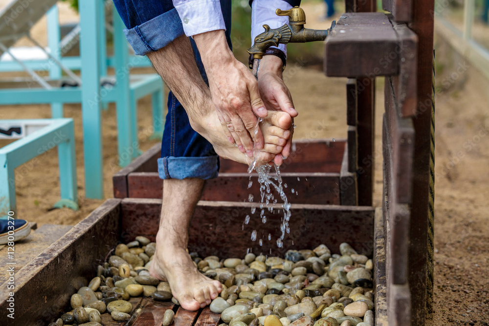 Man washing his feet on the sand beach. Place for washing the feet is ...