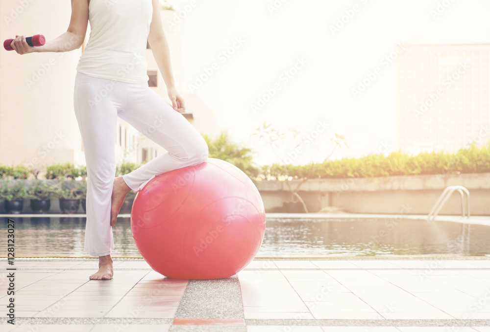 Young woman standing on red ball overlooking a swimming pool with sun ...
