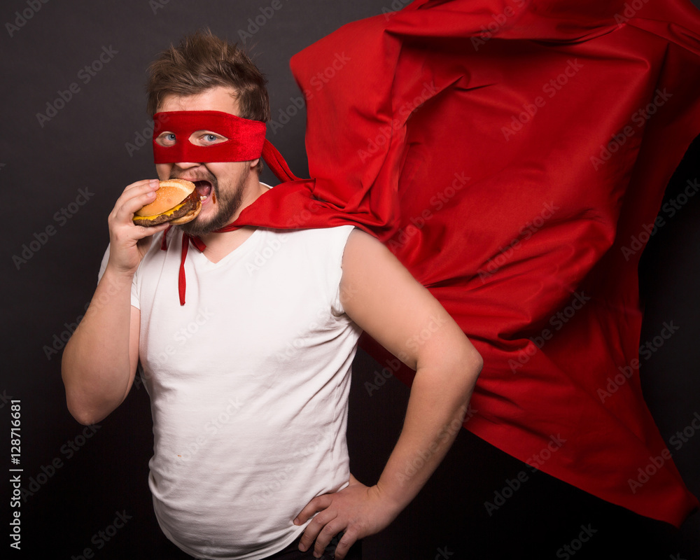 Super hero concept. Handsome man with red mask on eating hamburger ...