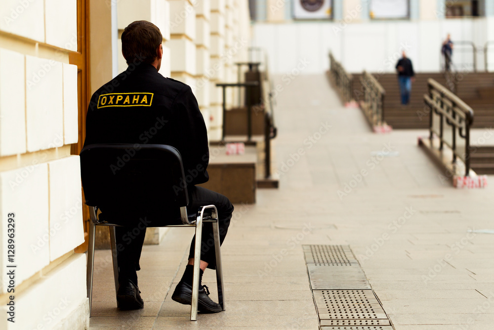 Security guard sitting on a chair at the entrance to the indoor Stock ...