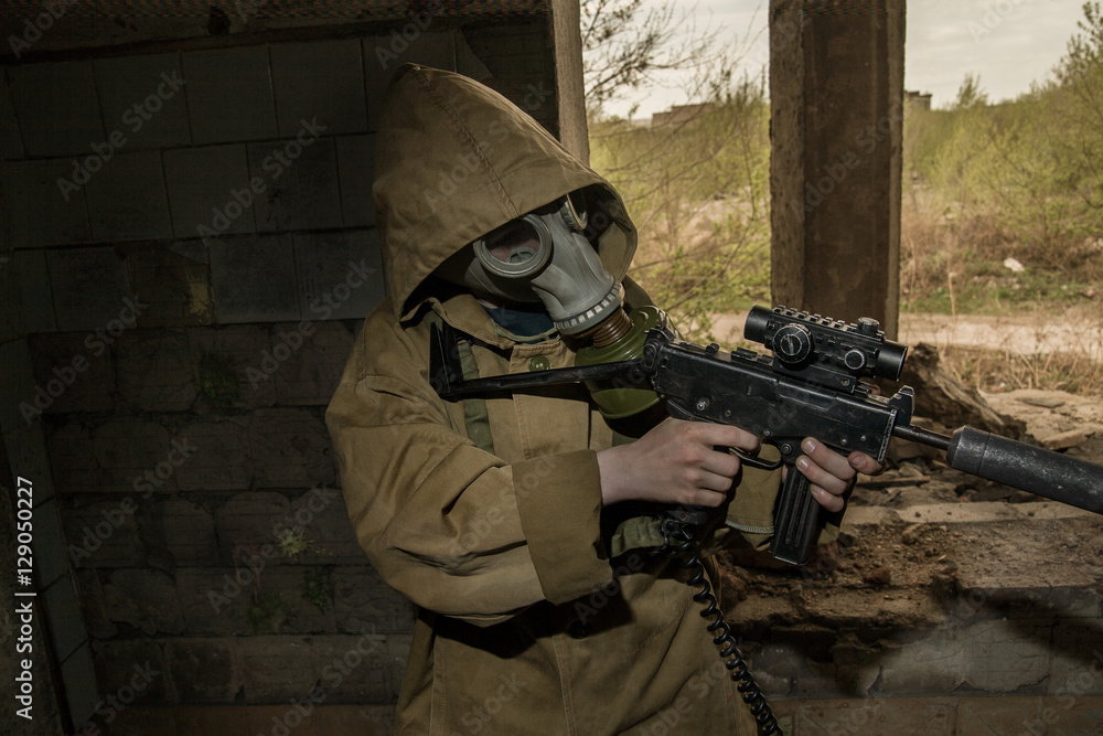 young boy stands with a gun in his hand. boy in a gas mask. boy in a ...