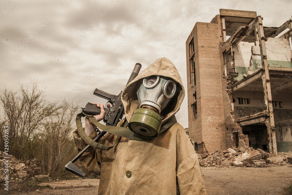 young boy stands with a gun in his hand. boy in a gas mask. boy in a ...