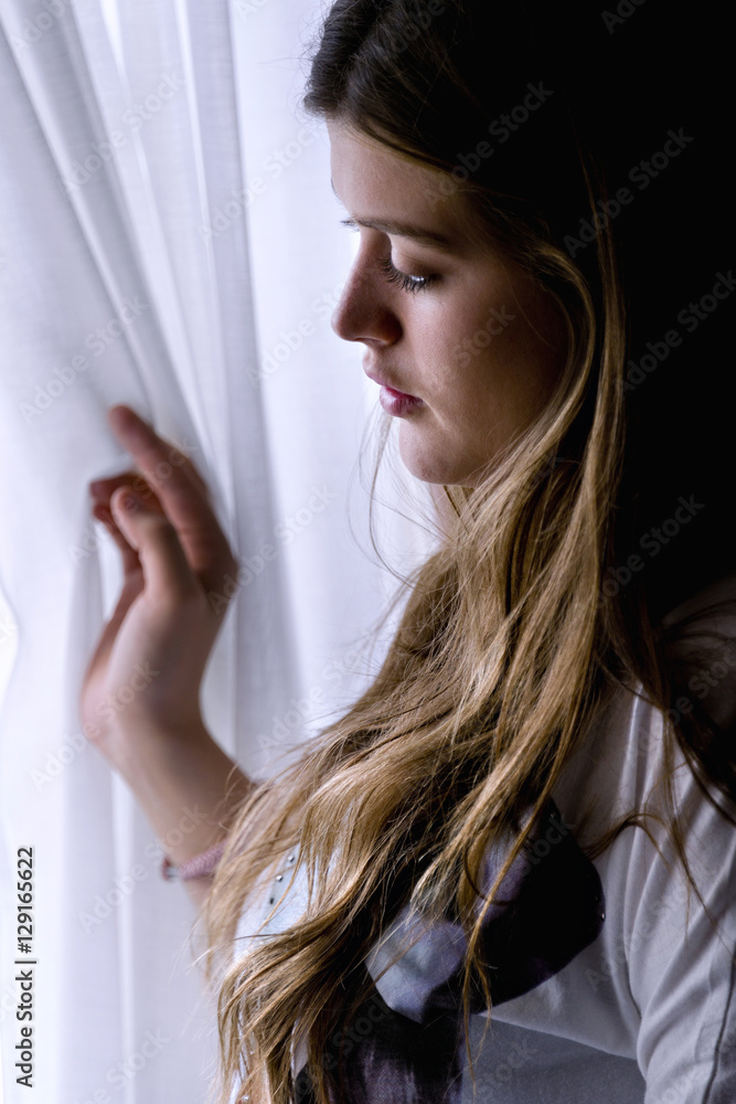 Teenage girl looking through a window, inside a house Stock Photo | Adobe Stock