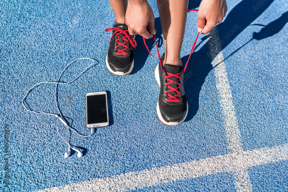Running motivation music on mobile phone runner woman tying shoe laces ...