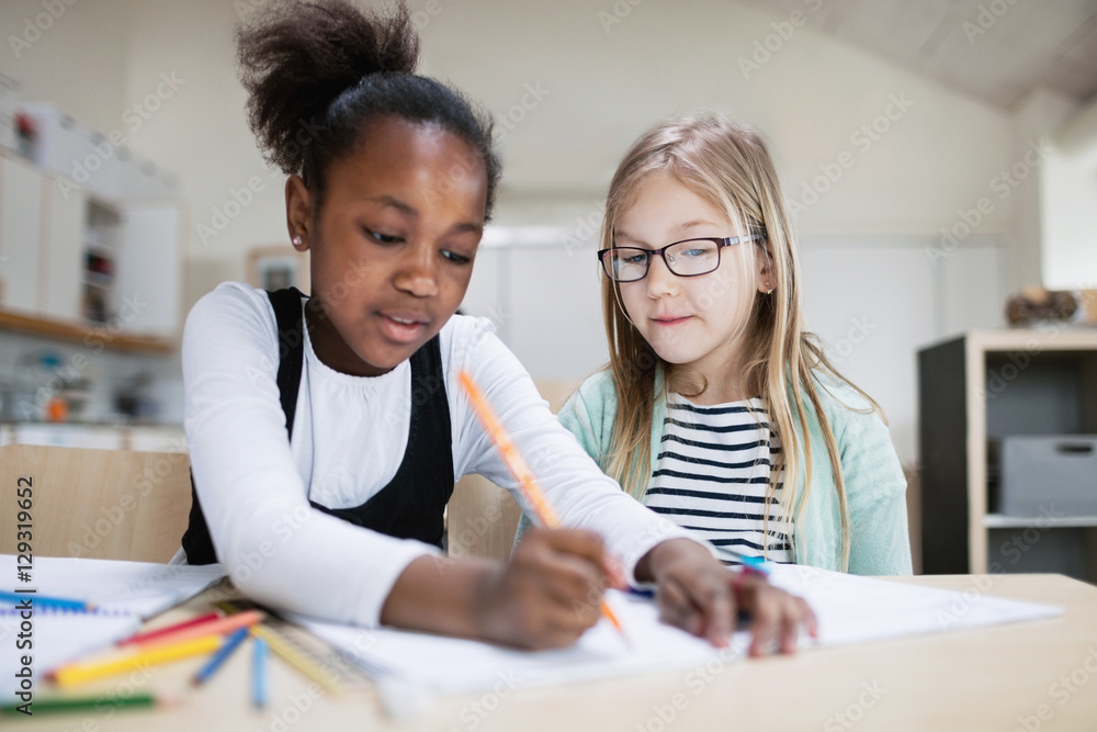 Girl assisting friend while studying in classroom at school Stock Photo ...