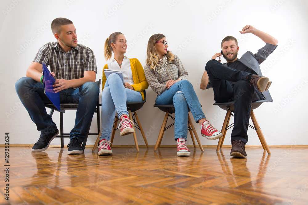 Group of frightened young people is sitting in a row in an office and ...