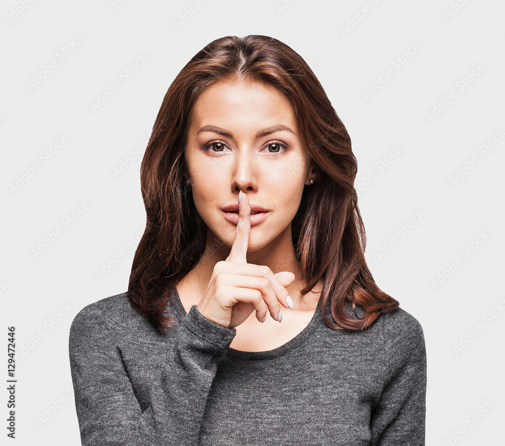 Young woman holding a finger on her lips - silent gesture. Close up of ...