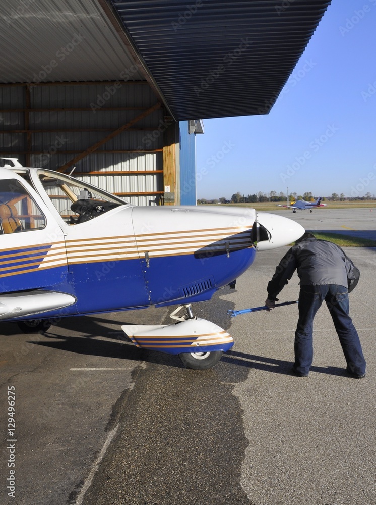person using a tow bar to pull a propeller airplane out of a hangar ...