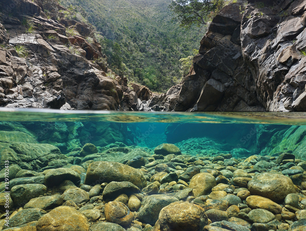 Rocks over and under the water split by waterline in a river with clear ...