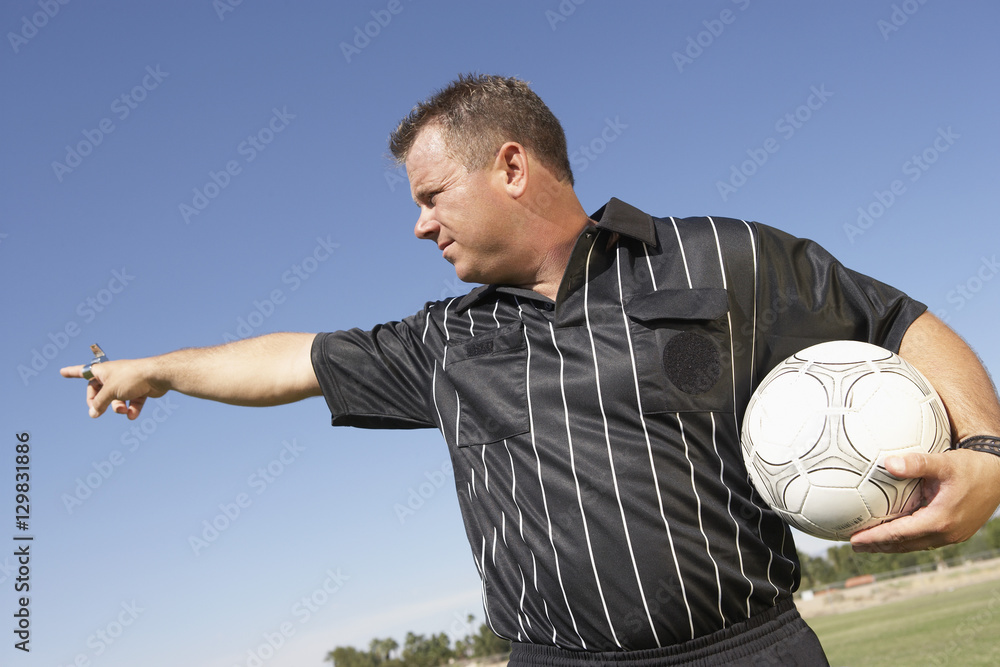 Mature male referee with soccer ball pointing at distance Stock Photo ...