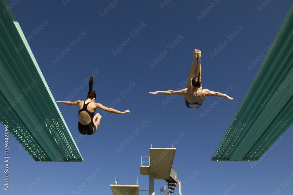 Rear view of two women diving from diving boards against clear blue sky ...