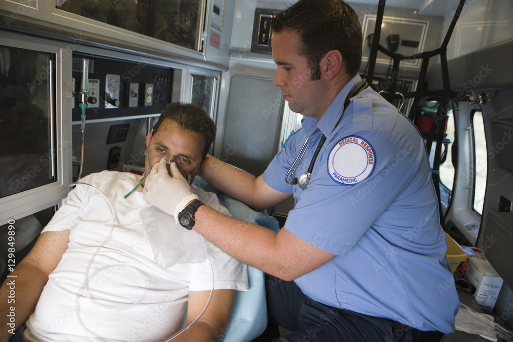 Male EMT professional helping man with oxygen mask inside ambulance ...