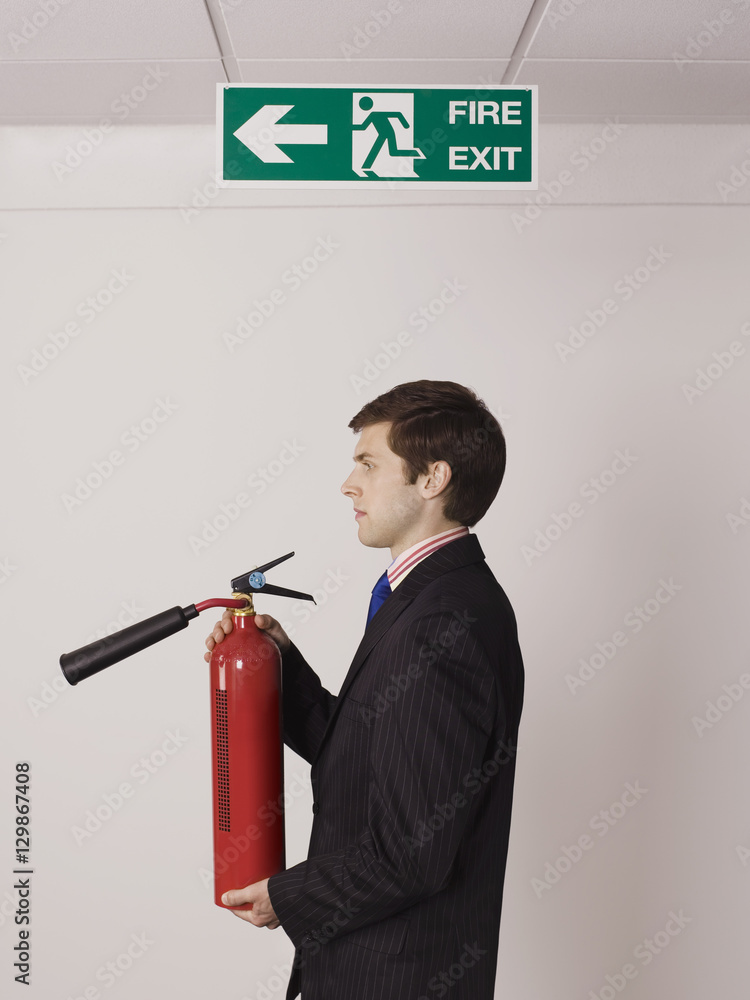 Side view of a young businessman holding fire extinguisher under exit ...