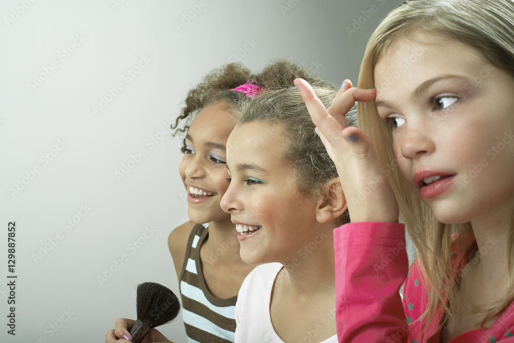 Closeup side view of three happy girls side by side putting on makeup ...