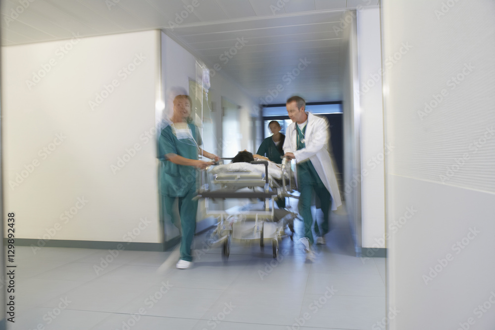 Medical workers moving patient on gurney through hospital corridor ...