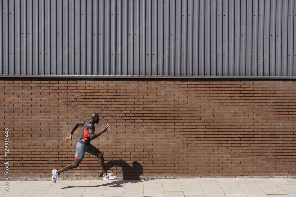 Side view of an African American man running by brick wall Stock Photo ...