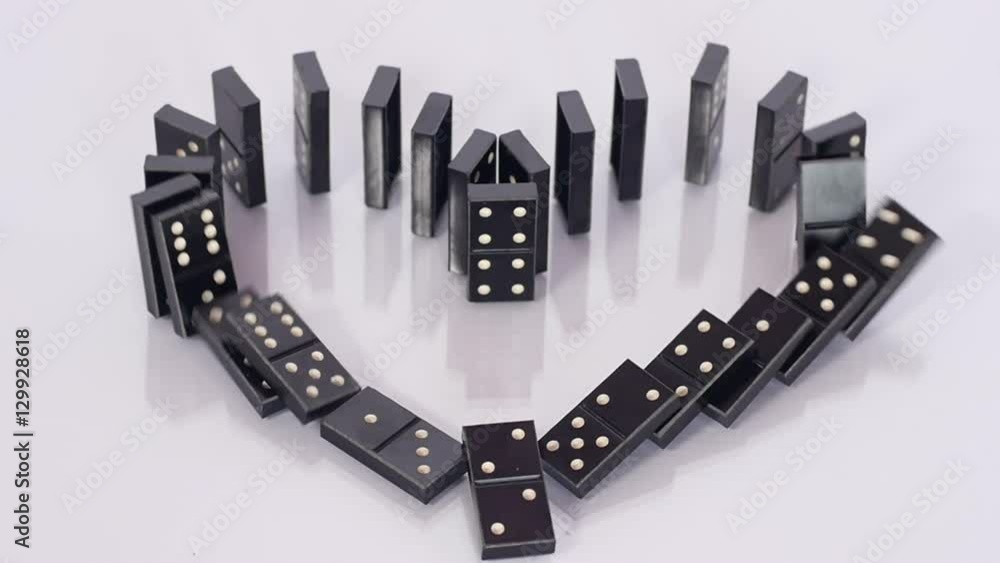 A finger pushes black domino and it causes whole chain to fall in shape ...