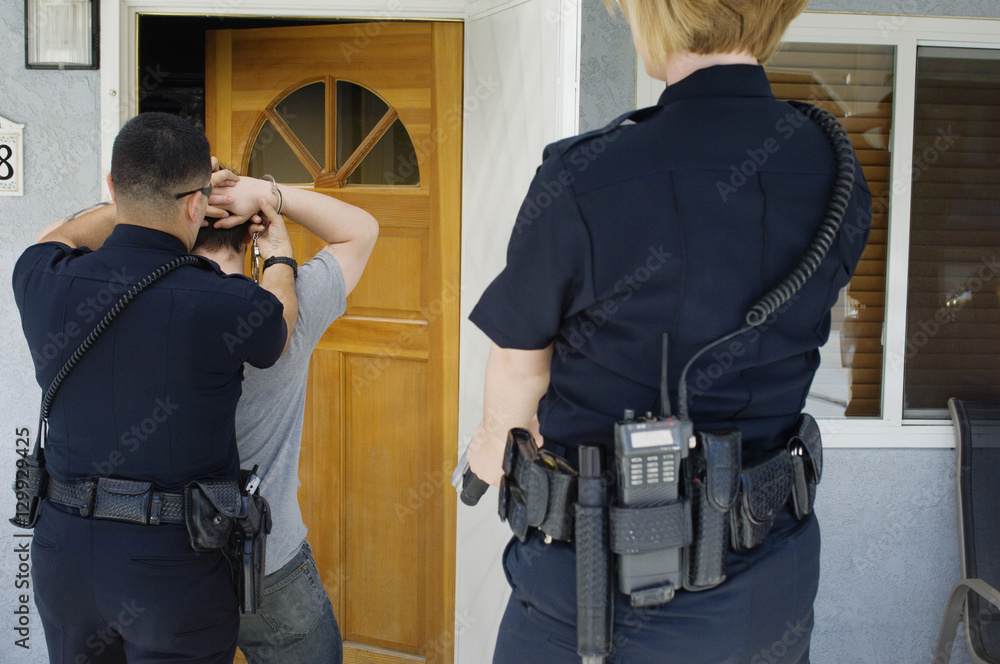Rear view of police officers arresting young man outside house Stock ...