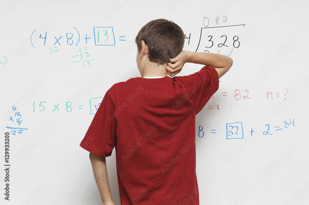 Rear view of a teenage boy scratching head against white board in ...