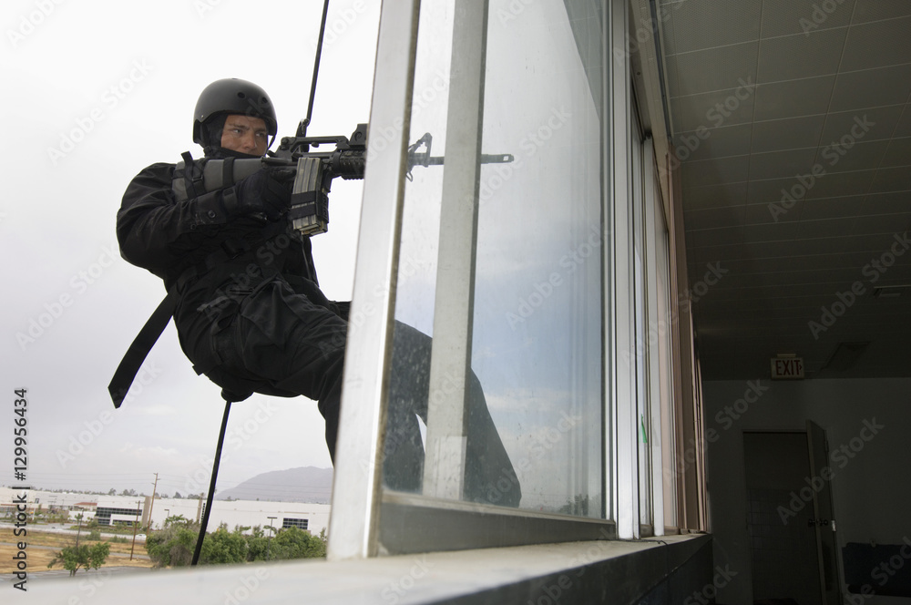 SWAT team officer rappelling and aiming gun through glass window Stock ...