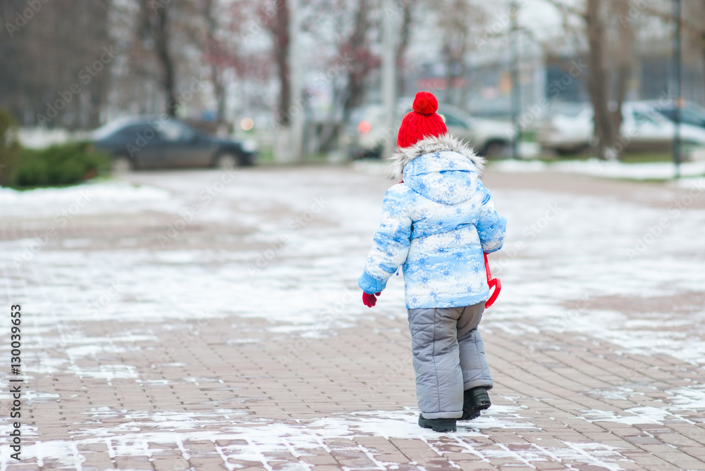 Little girl in the winter suit is on the square. We see the back Stock ...