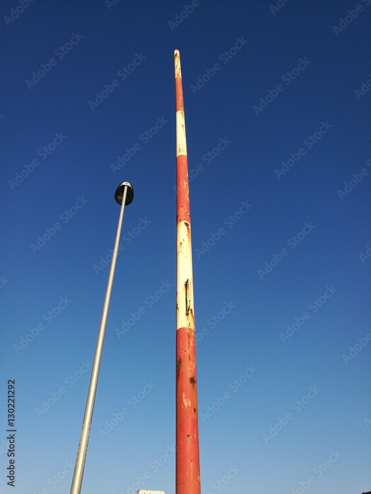 Rostiger alter Schlagbaum in Rot und Weiß vor strahlend blauem Himmel ...