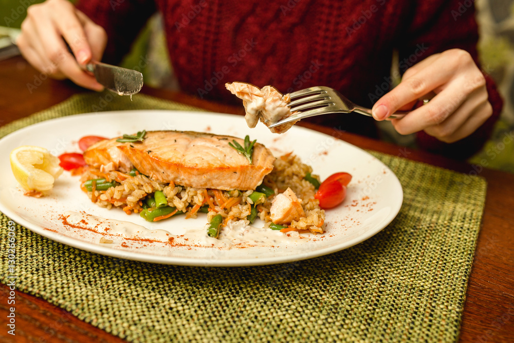 Girl with fork and knife in the hands eating salmon steak with rice and ...