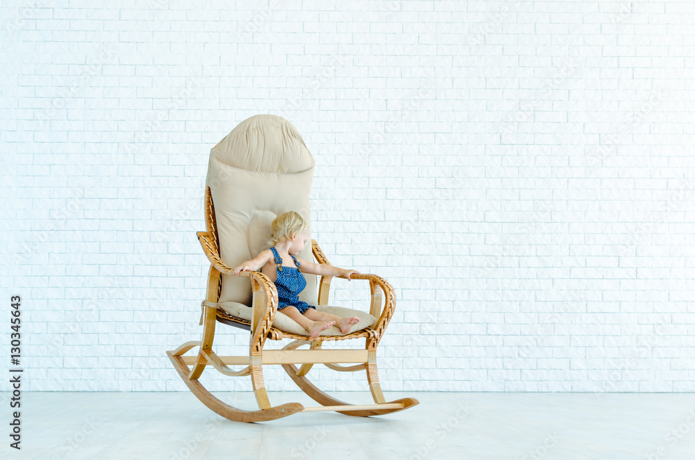 Little girl rides a rocking chair on the background of a white brick ...