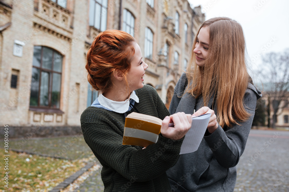 Happy two girls reading book together at university campus Stock Photo ...