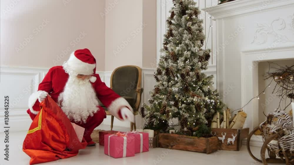 Santa Claus putting presents back into his bag by Christmas tree Stock ...