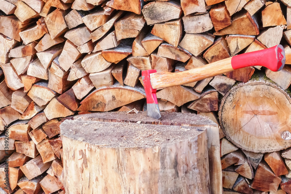 Red handled axe stuck into a stump on stacked firewood background Stock ...