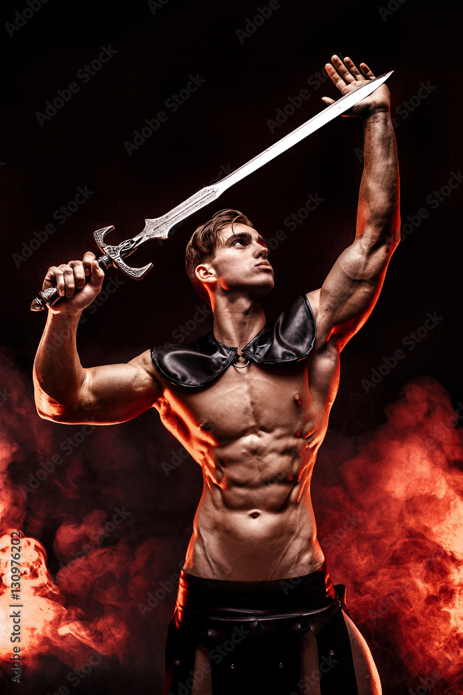 Young muscular model posing with sword in hands and looking away in ...