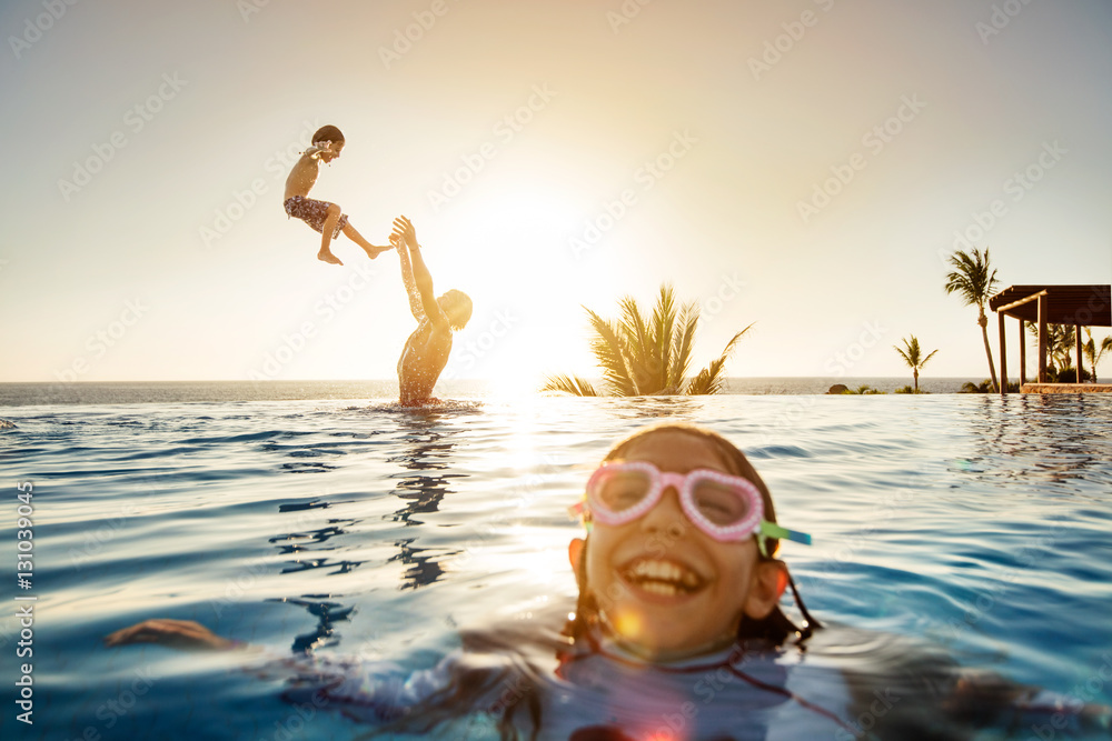 Father throws son in the pool with daughter in forground wearing ...