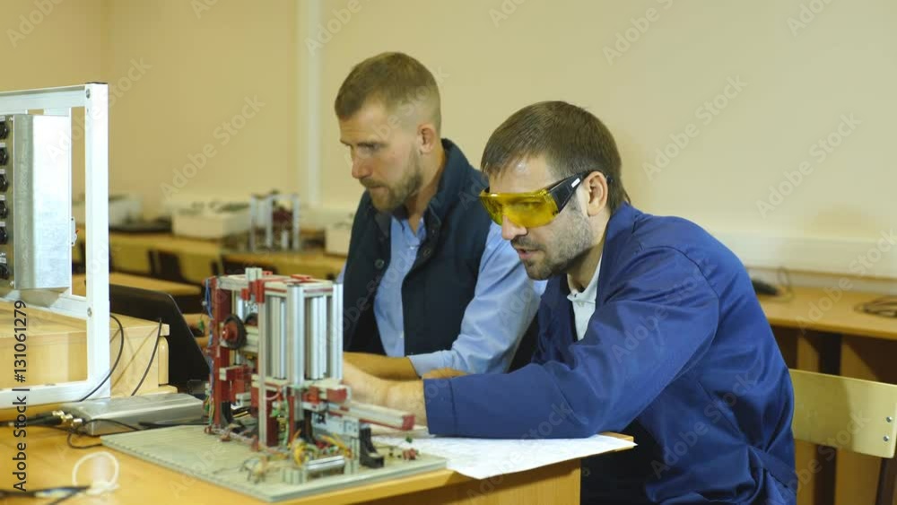 Engineering working in the lab, adjusting a 3D printer's components ...