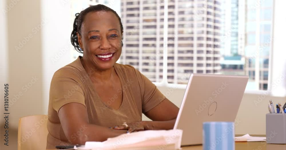 A portrait of an older black woman at work using her laptop. An elderly ...