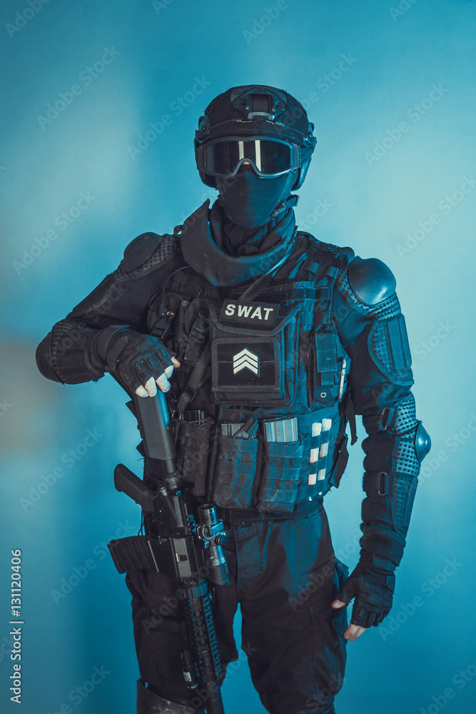 Member of the SWAT squad with an assault rifle in a black uniform on blue background. Special ...