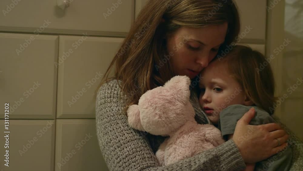 Sad, scared young girl with a stuffed animal being held by her mother ...