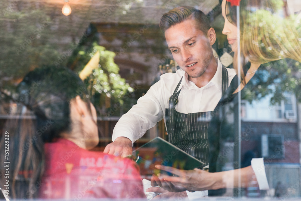 Window view of bartender and young women pointing at menu in cocktail ...