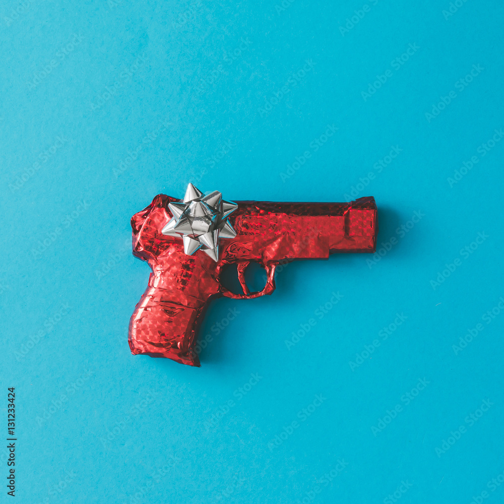 Gun wrapped in red paper with bow on blue background. Flat lay C Stock ...