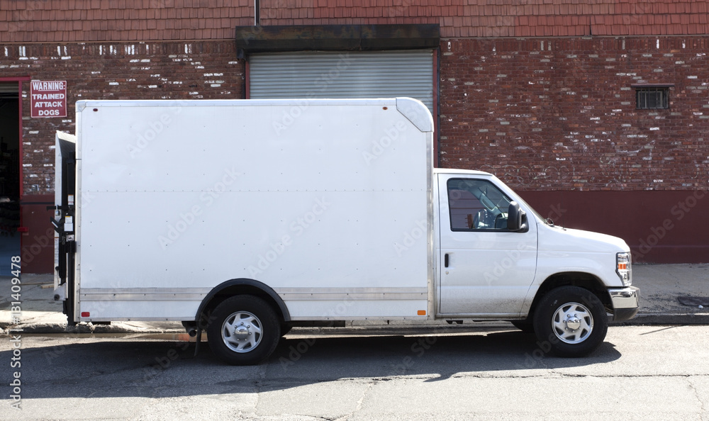 Parked white delivery truck in front of brick building. Horizontal ...