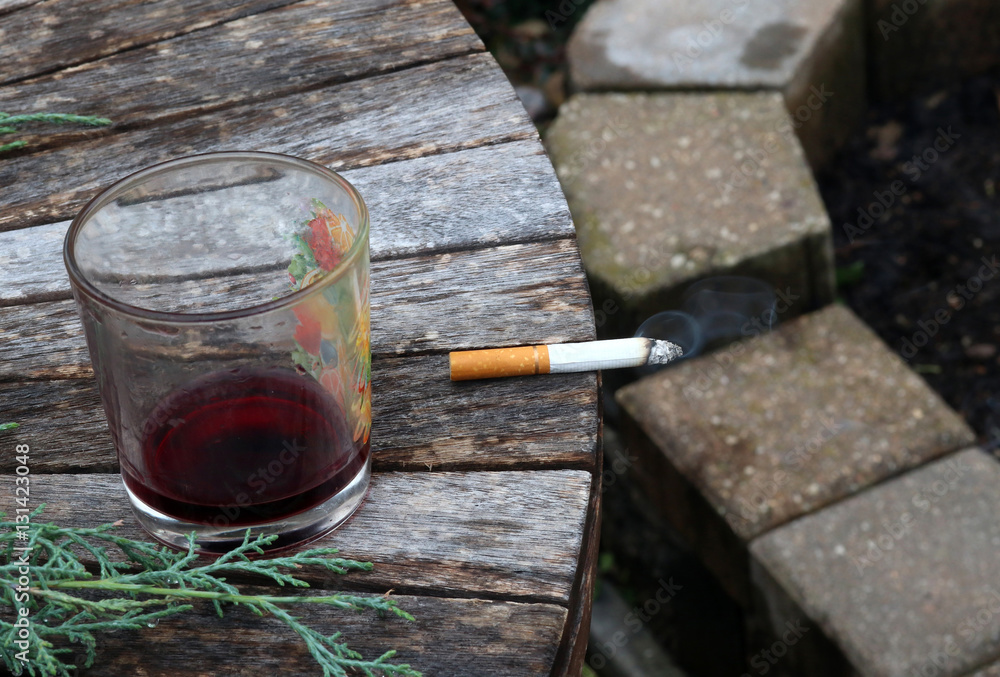 Burning cigarette with ash and smoke left on the outdoor wooden table ...
