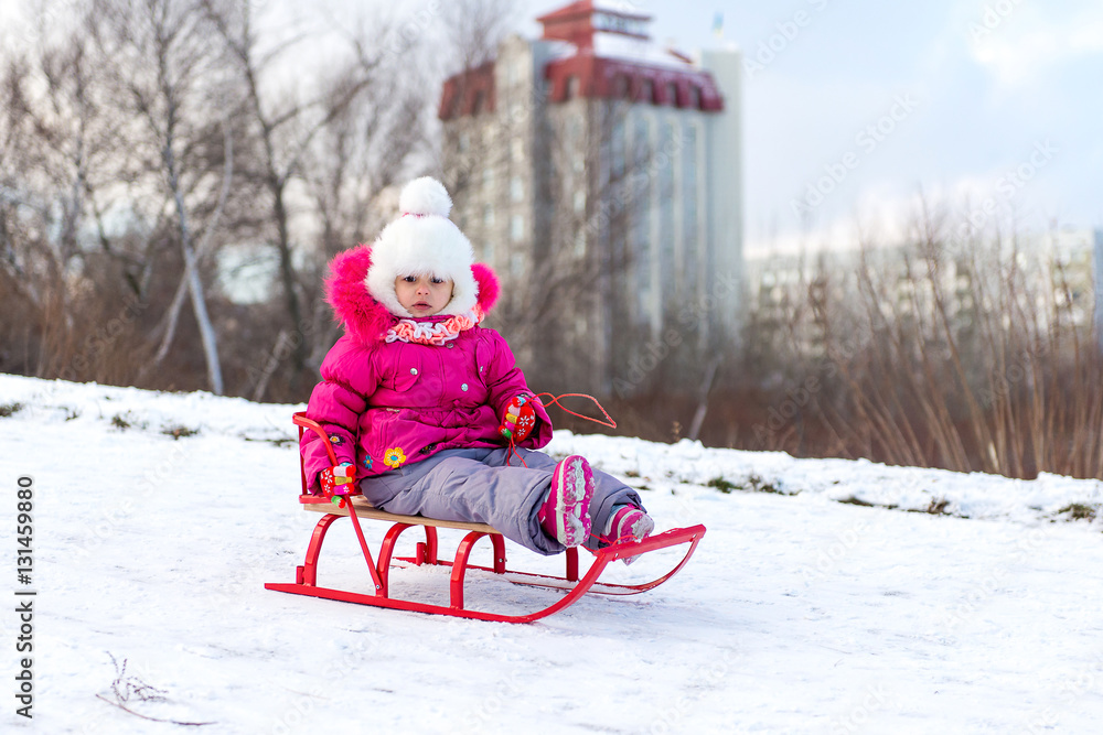 The child, a little girl riding on a sled with snow slides. Winter fun ...