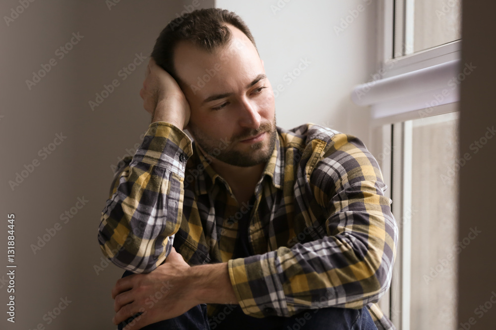 Handsome depressed man sitting near window Stock Photo | Adobe Stock